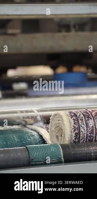 A patterned carpet moves through industrial rollers while a worker ...