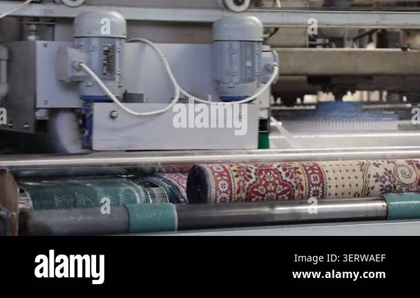 A patterned carpet moves through industrial rollers while a worker ...