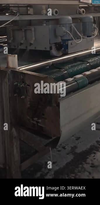 A patterned carpet moves through industrial rollers while a worker ...