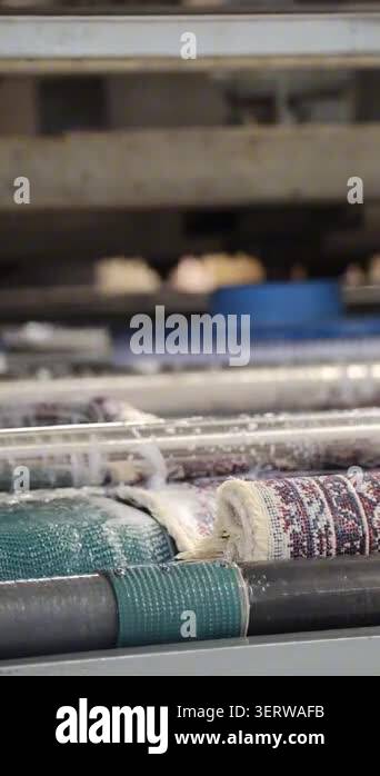 A patterned carpet moves through industrial rollers while a worker ...