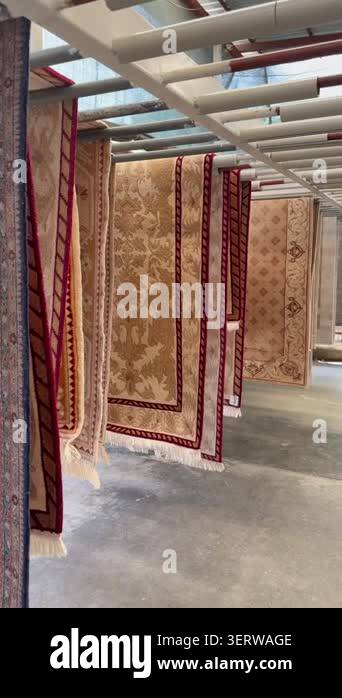Rows of patterned rugs hang from ceiling rails in a spacious indoor ...
