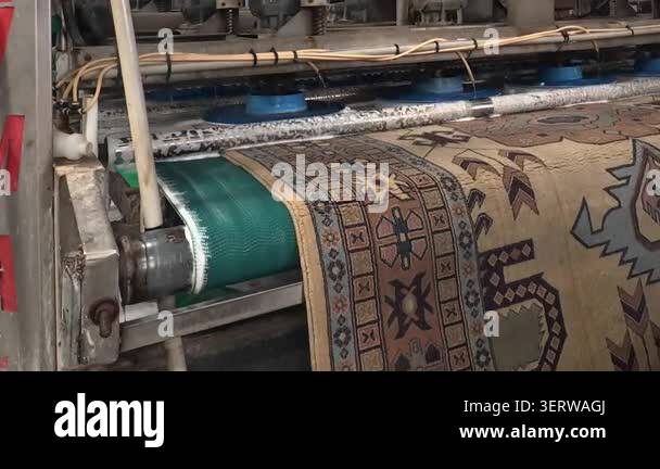 A patterned carpet moves through industrial rollers while a worker ...