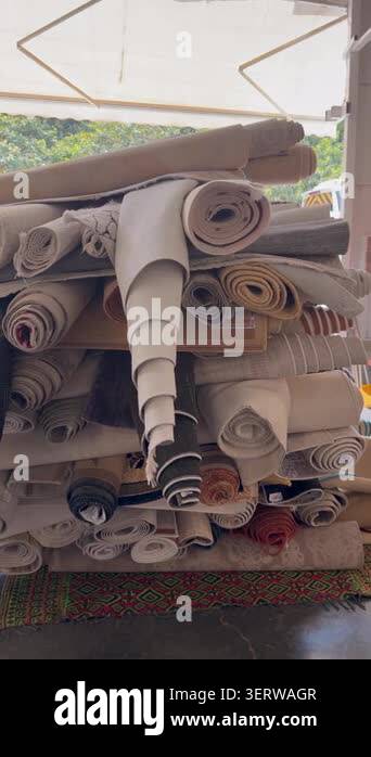 A tall arrangement of rolled carpets and rugs stands inside a market ...