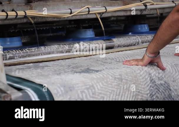 A patterned carpet moves through industrial rollers while a worker ...
