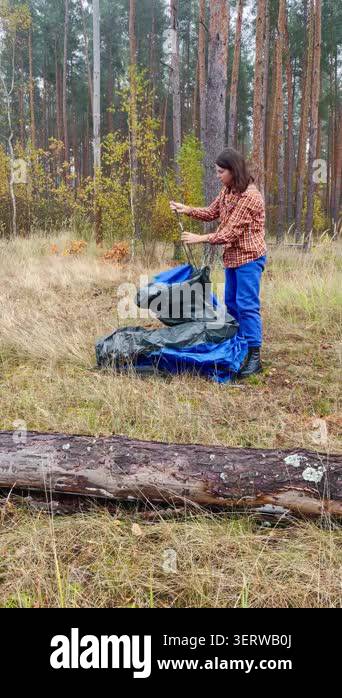 A young woman is setting up a tent in a woodland environment ...