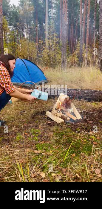 A young woman in a plaid shirt carefully adds kindling to a small ...