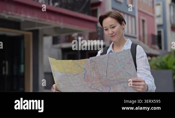 Portrait of happy female tourist holds map and looks around near old ...