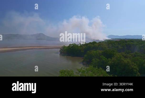 Aerial view of smoke rising from a fire near a coastline with lush ...
