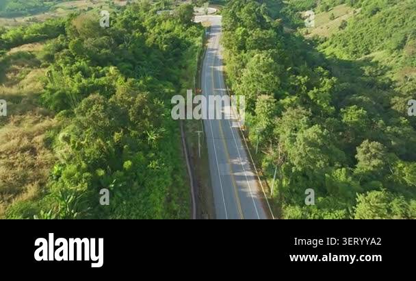 Aerial drone footage flying over a winding road through lush green ...
