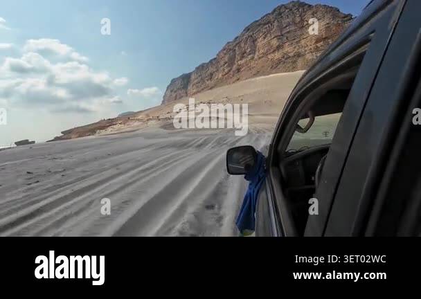 View from a car driving on a sandy desert road beside rocky cliffs ...
