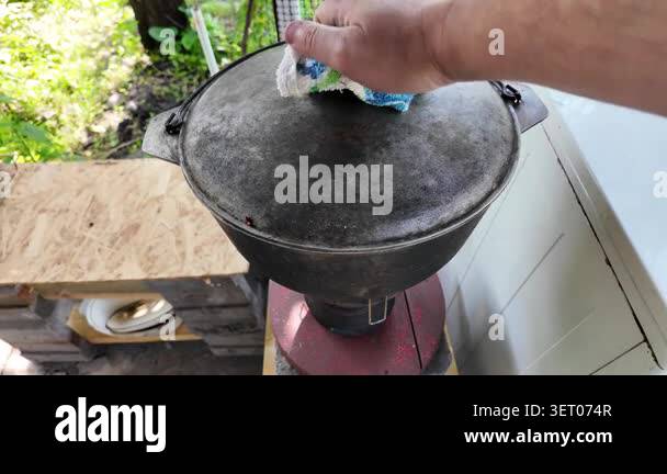 Male hand stirring hot boiling meat stew with a spoon in a large cast ...