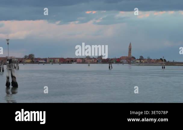 Calm coastal scene with water, wooden pillars, pastel buildings, cloudy ...