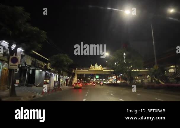 Night street drive under illuminated arch with slowmoving traffic and ...