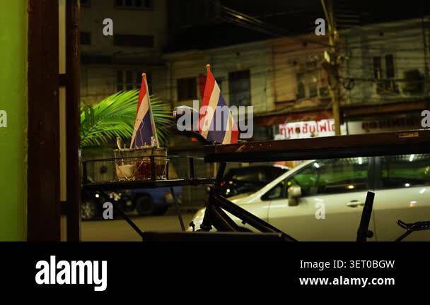 Nighttime thailand street with flags showing delivery rider waiting by ...