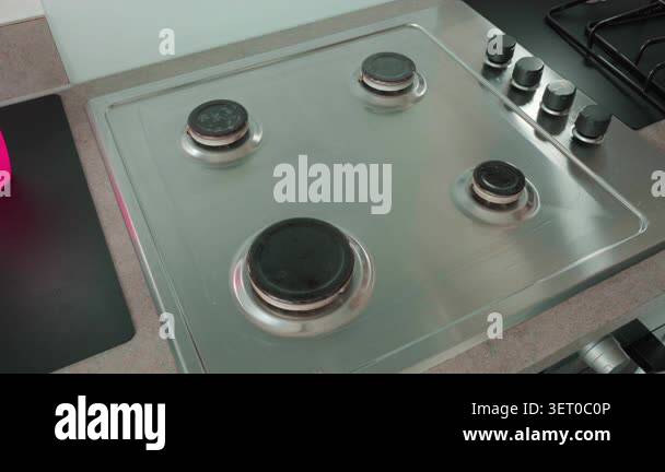 Hand cleans stove burner with green cleaning sponge. Stove has four ...