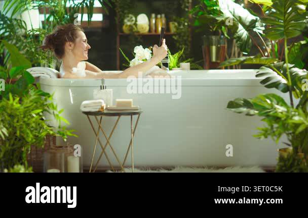 A smiling woman with a bun enjoys a luxurious bubble bath, using a ...