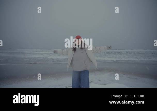A woman in a red beanie and white jacket stands on a winter shoreline ...