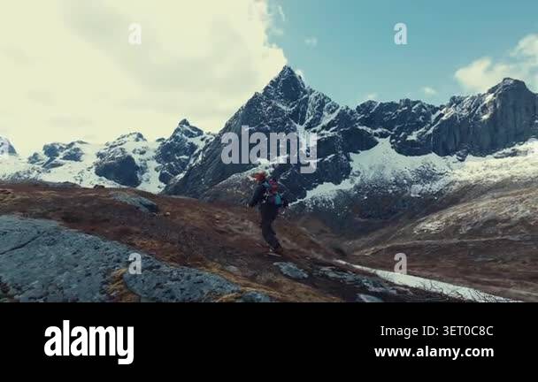 A lone hiker with a red backpack moves along a rocky high altitude ...