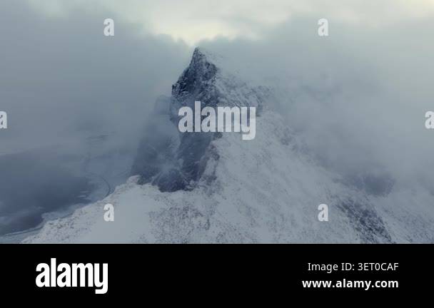 A jagged mountain summit covered in snow rises through thick drifting ...