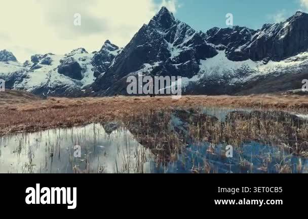 A solitary hiker stands on a grassy, marshy plain dotted with shallow ...