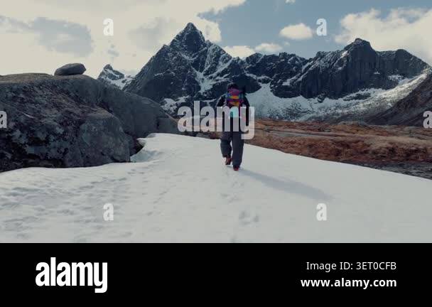 A lone hiker walks away across a snow-covered mountain ridge surrounded ...