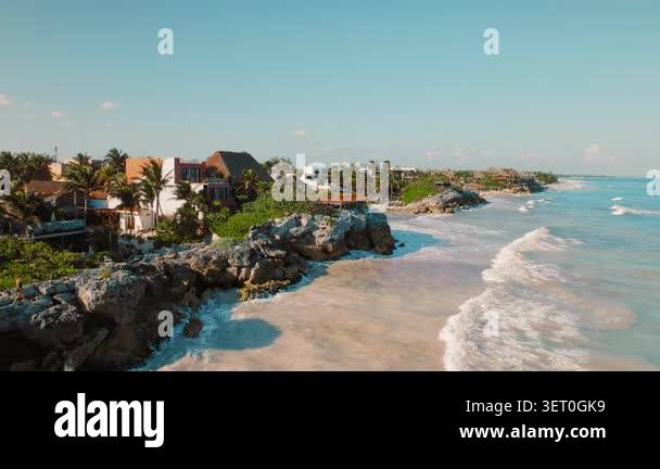 Woman walks on cliffs beside ocean surf in tropical seaside village ...