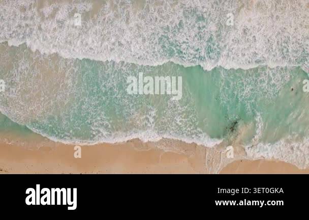 Top down view of turquoise sea waves lapping against golden sand beach ...