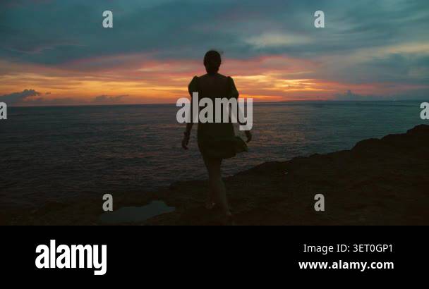 Silhouette of woman walking on cliff edge watching beautiful warm ...