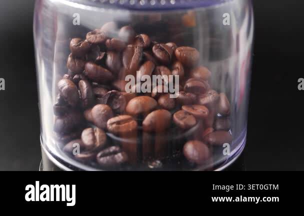 Roasted coffee beans spinning in a transparent grinder bowl on a dark ...