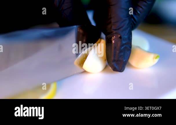 Close-up of a chef cutting fresh garlic on a white porcelain board with ...