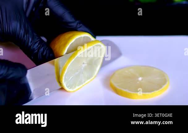 Close-up of a chef cutting fresh lemon into thin slices on a white ...