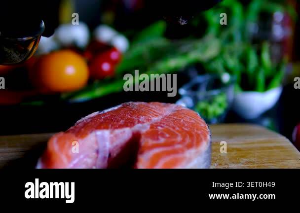 Chef in black gloves seasons salmon, sears it on a stainless steel pan ...