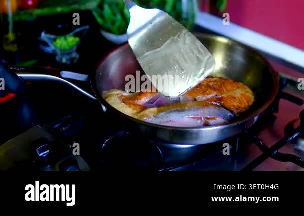 Chef in black gloves seasons salmon, sears it on a stainless steel pan ...