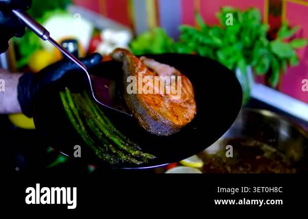 Chef in black gloves seasons salmon, sears it on a stainless steel pan ...
