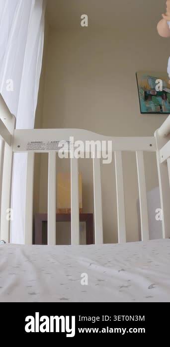 Mom gently puts her 6 months old baby boy into a crib at home, creating ...