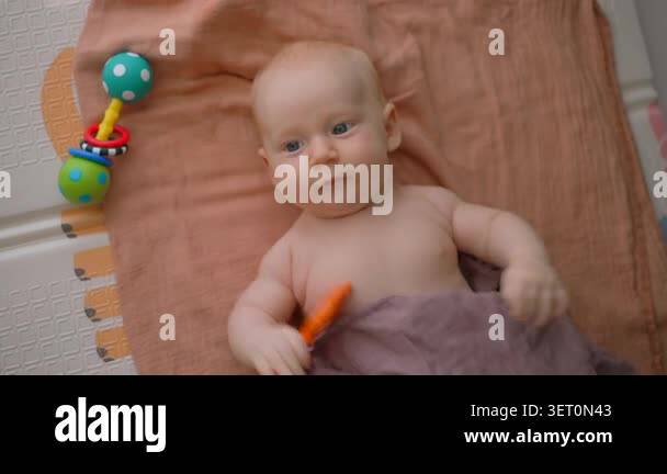 Three month old baby lies on a soft mat on the floor at home, covered ...