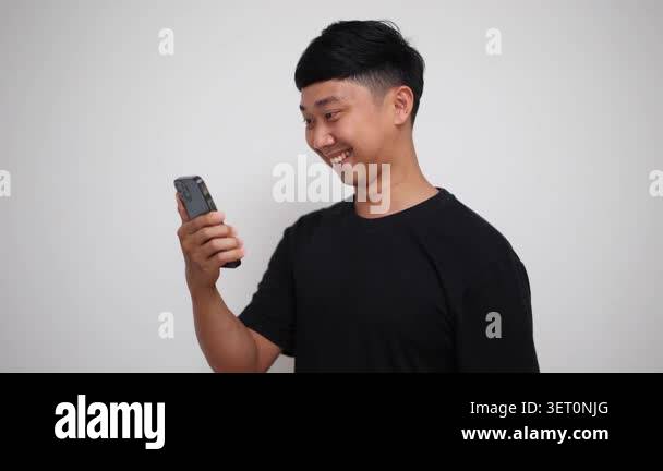 Young Asian man looking at his smartphone, smiling, celebrating success ...
