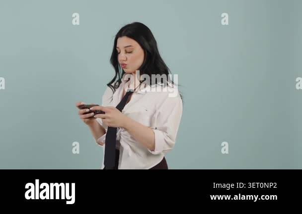 A focused young woman stands against a blue background playing a video ...