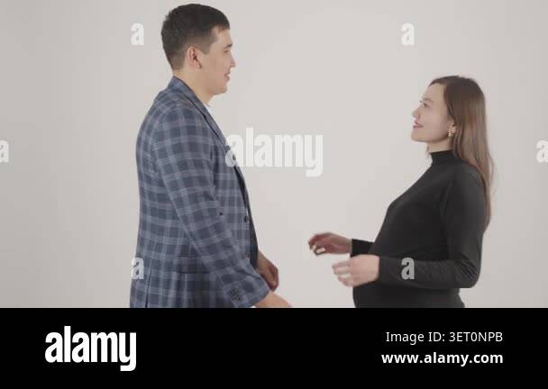 A happy expectant couple embraces affectionately against a plain ...