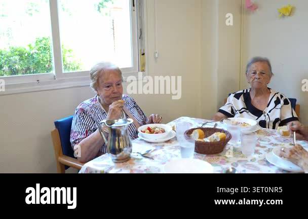 Two senior women sitting at a table having lunch in a retirement ...
