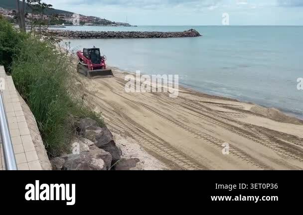 Landscape 4K view of a tractor leveling and grooming the sandy shore at ...