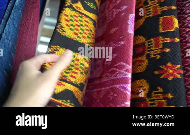 Hand touching rows of colorful traditional Thai silk fabrics, close up ...