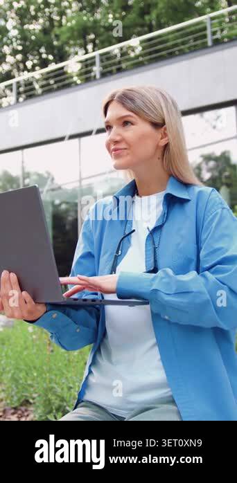Side view of a focused woman with blond hair sitting on a bench outside ...