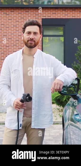 Handsome bearded man in a white shirt charging an electric car and ...