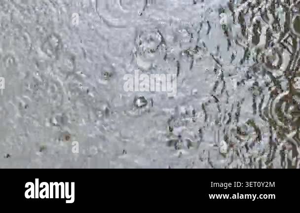 Raindrops falling into water and a puddle, creating circular ripples ...
