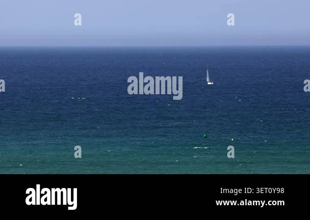 A sailboat glides across the deep blue ocean, with a kite surfer ...