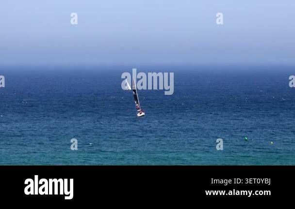 Two sailboats race across the deep blue ocean under a hazy sky. The ...