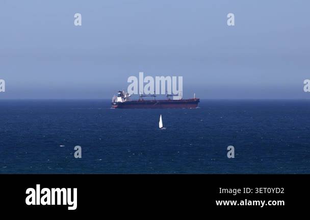 A large cargo ship sails across the deep blue ocean, with a small ...