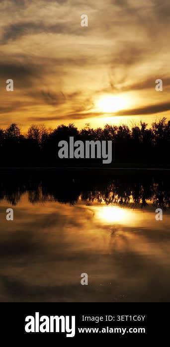 A golden-hued lake glows minutes before sunset, reflecting vegetation ...