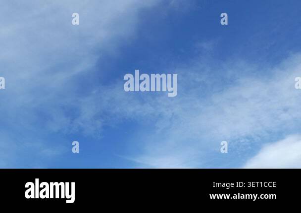 Static wide shot captures a bright blue sky filled with wispy white ...
